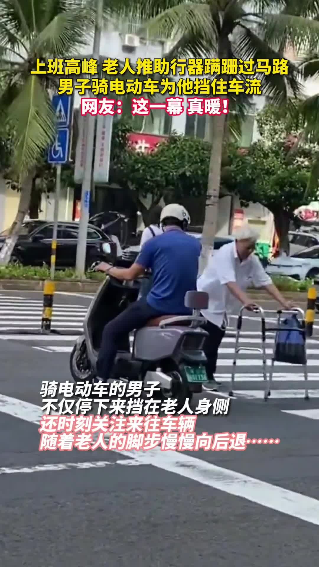 上班高峰,老人推助行器蹒跚过马路,男子骑电动车为他挡住车流。