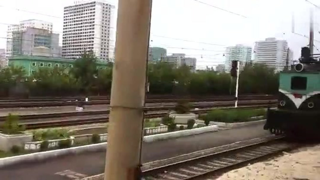 国际列车缓慢驶出平壤火车站铁路边街景清晰可见