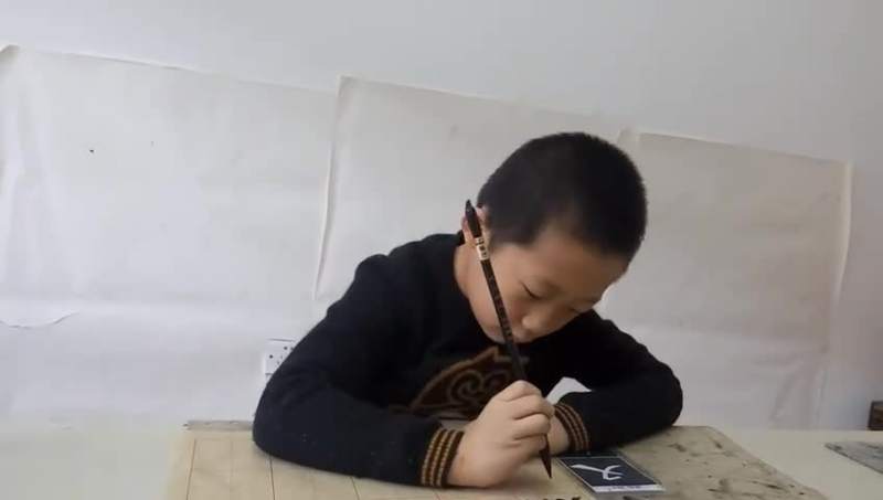 这个小男孩练习毛笔字,正确端正的握笔,表情认真、全情投入