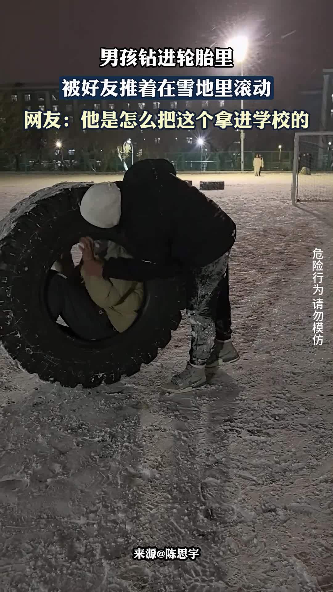 男孩钻进轮胎里,被好友推着在雪地里滚动。
