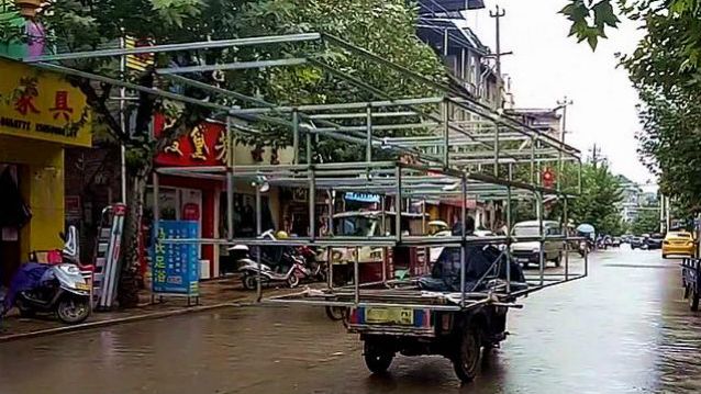 这小哥好牛X,用三轮电动车载着比车身大好几倍的架子当街穿梭