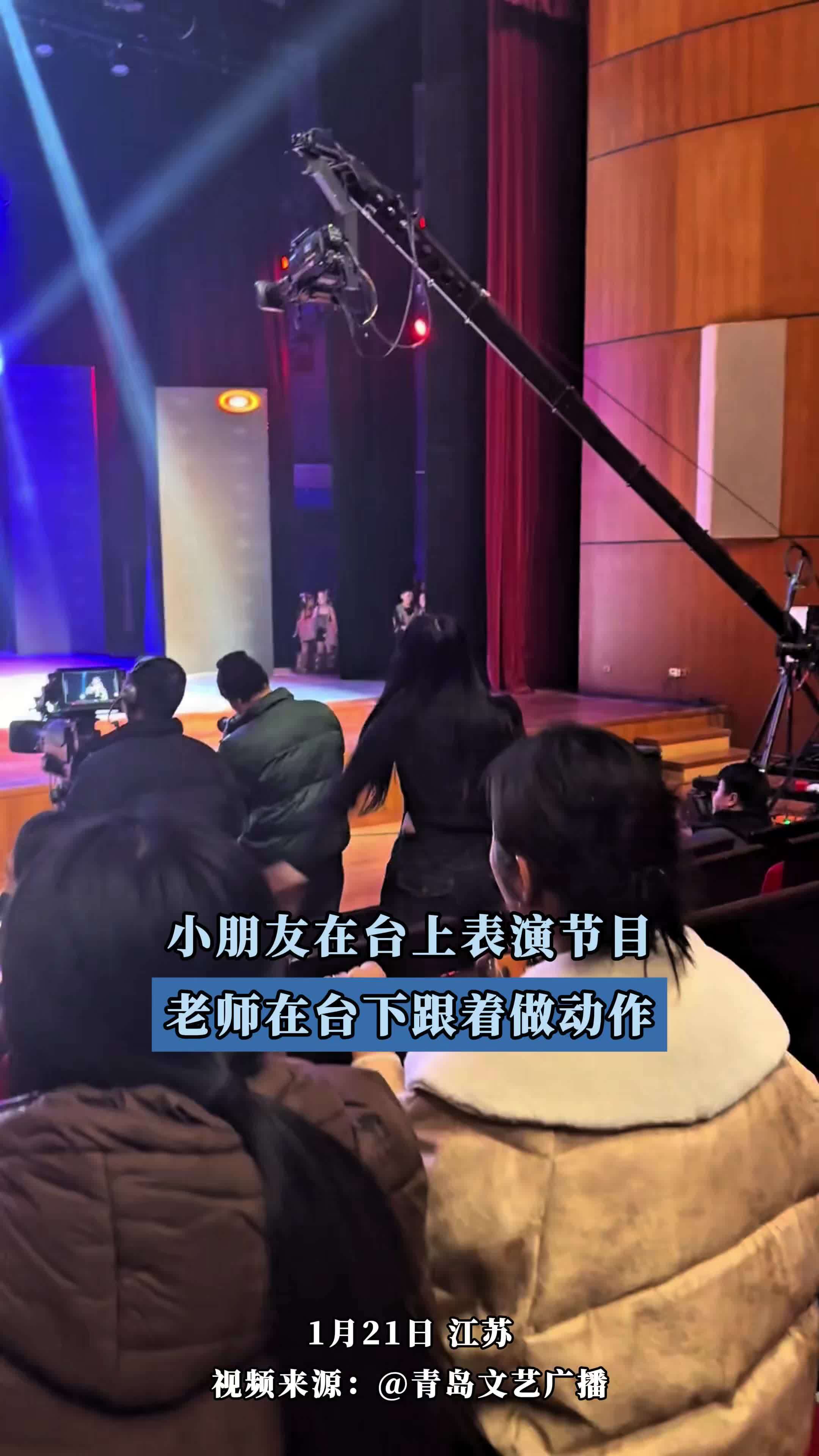 小朋友在台上表演节目,老师在台下跟着做动作