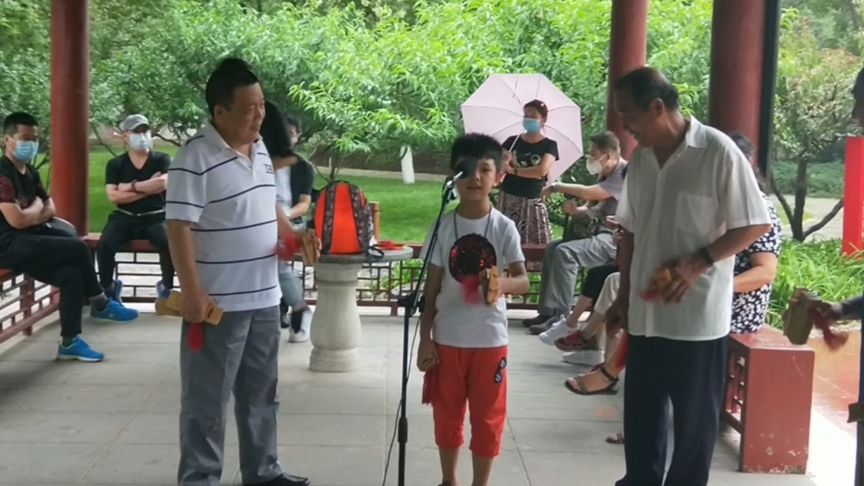 小学生在公园说快板,引来游客观看。