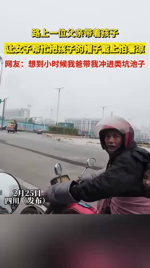 路上一位父亲带着孩子,让女子帮忙把孩子的帽子戴上怕着凉