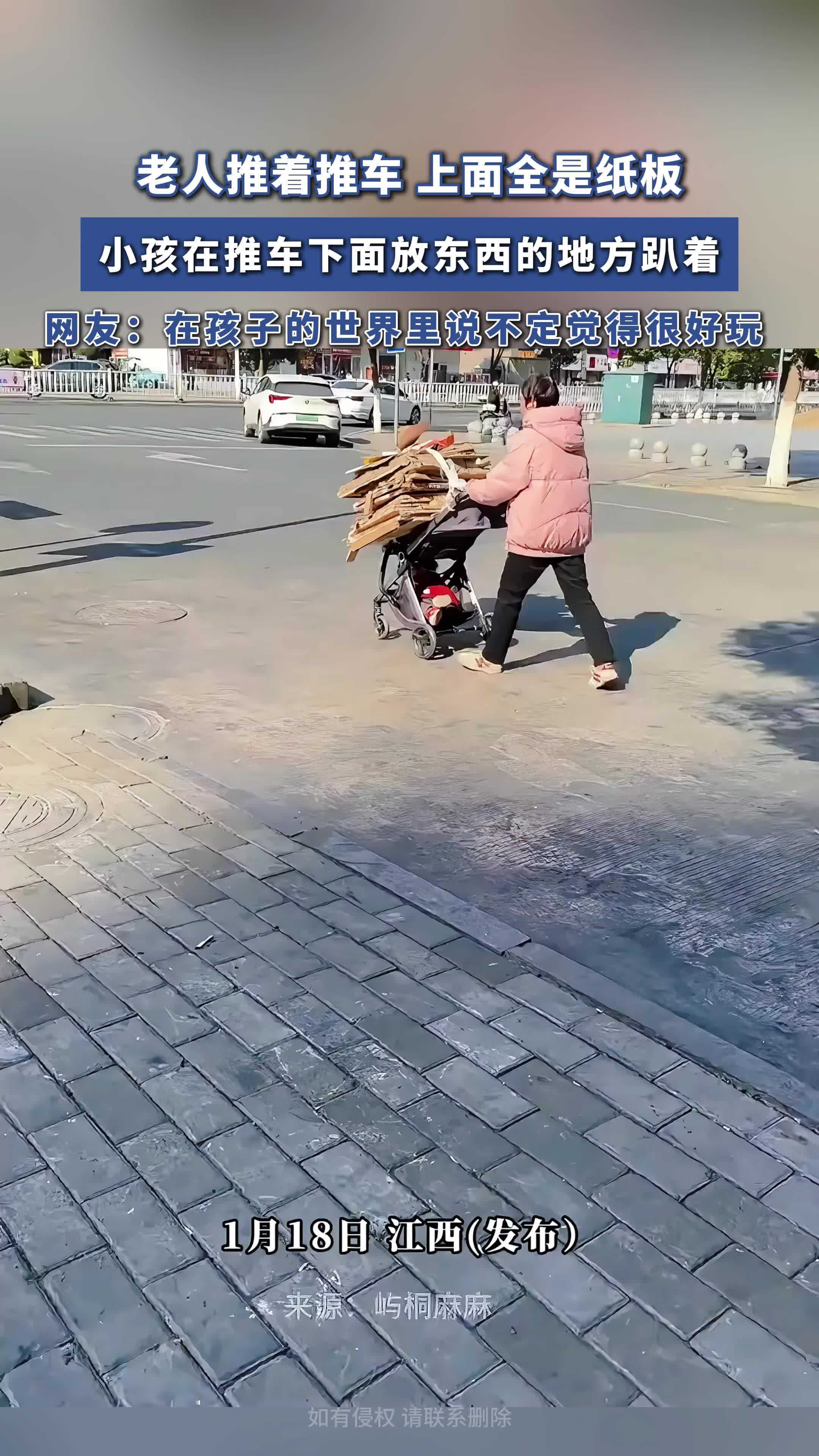 老人推着推车,上面全是纸板,小孩在推车下面放东西的地方趴着