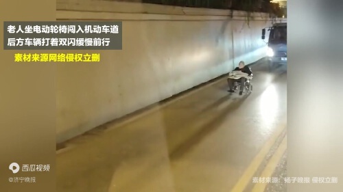 老人坐电动轮椅闯入机动车道,后方车辆打着双闪缓慢前行