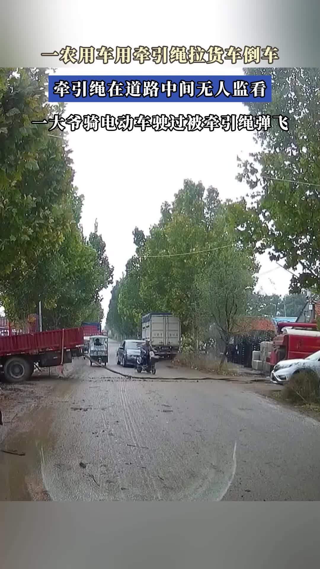 一农用车用牵引绳拉货车倒车,一大爷骑电动车驶过被牵引绳弹飞