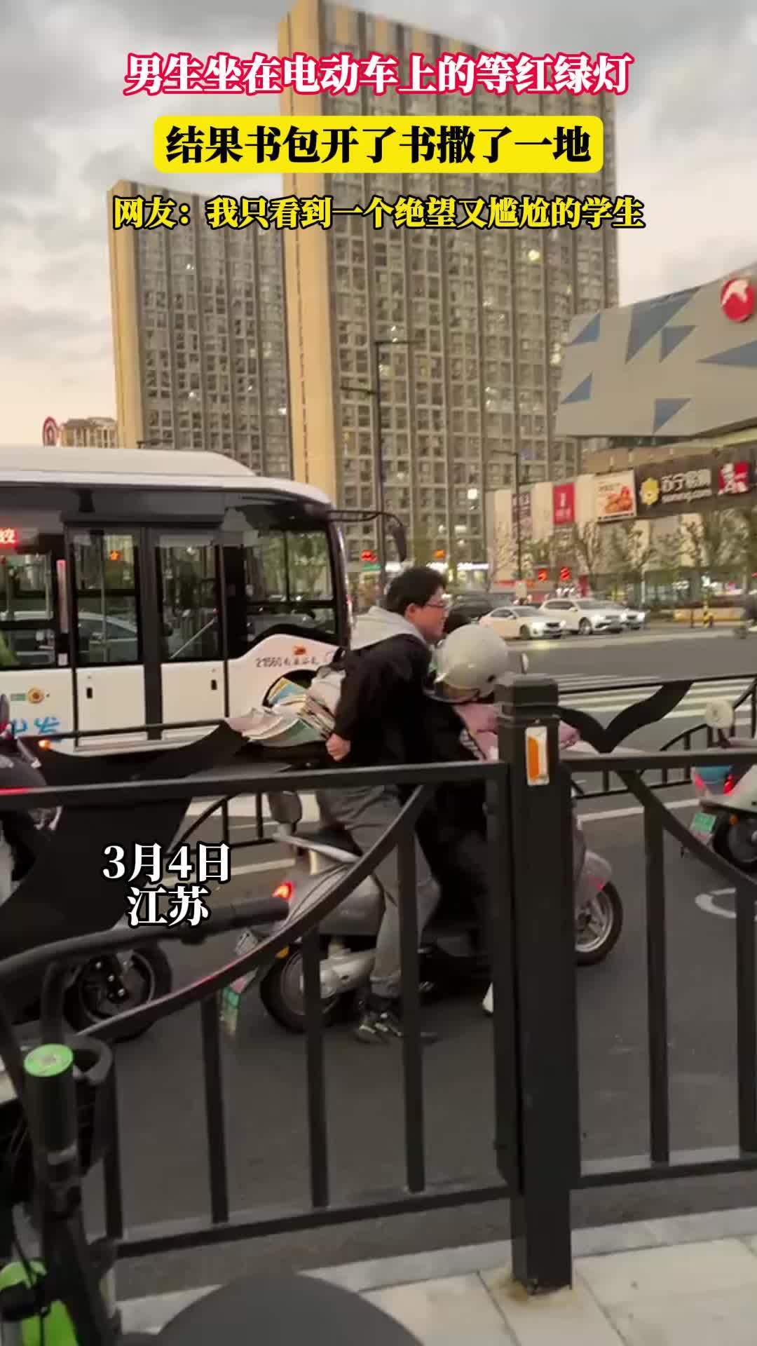 男生坐在电动车上的等红绿灯,结果书包开了书撒了一地