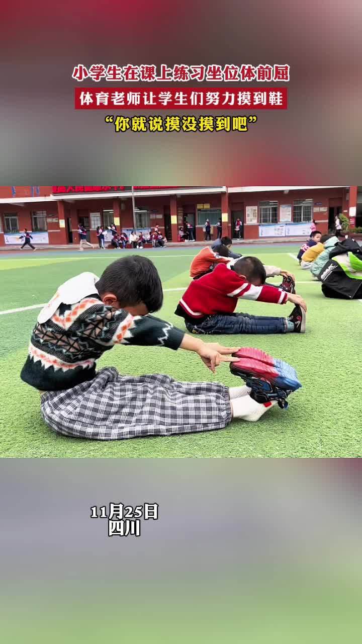 小学生在课上练习坐位体前屈,体育老师让学生们努力摸到鞋
